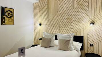 Cama bem arrumada com lençóis brancos e duas almofadas, parede com padrão geométrico de madeira, quadro na parede e dois luminários fixados na parede.