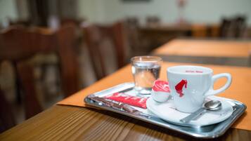 Uma bandeja com uma xícara branca, pires e colher, um copo de água e um guardanapo vermelho sobre uma mesa de madeira em uma sala de jantar.