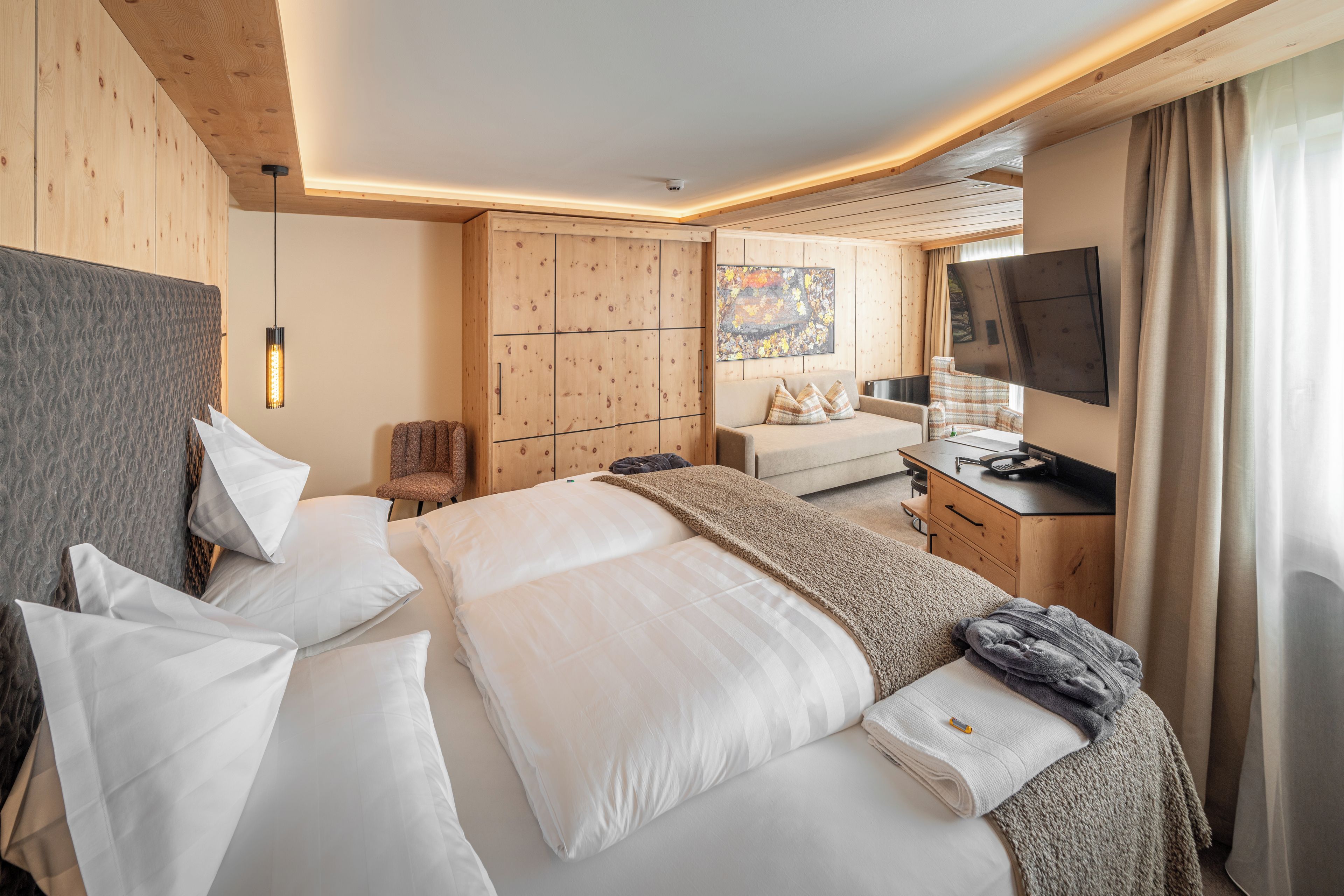 Quarto de hotel com uma cama grande, uma escrivaninha com TV de tela plana, uma cadeira e um sofá.
