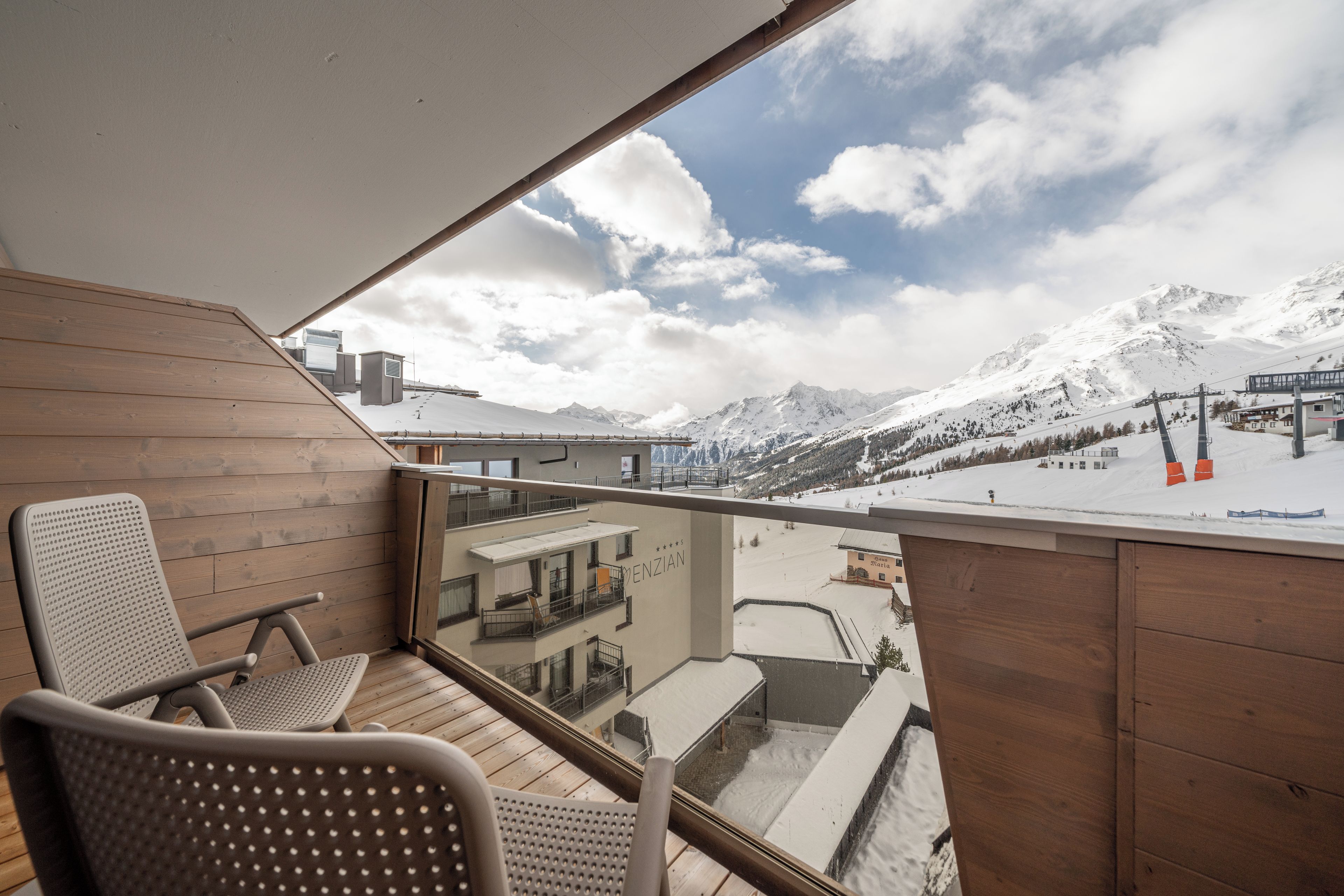 Varanda com vista para uma paisagem montanhosa coberta de neve, incluindo um teleférico e edifícios.