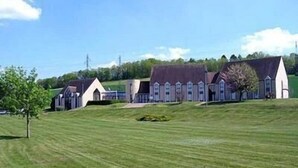 Uma fileira de edifícios tradicionais com telhados íngremes, possivelmente um local histórico ou religioso, situada em um campo gramado sob um céu claro.