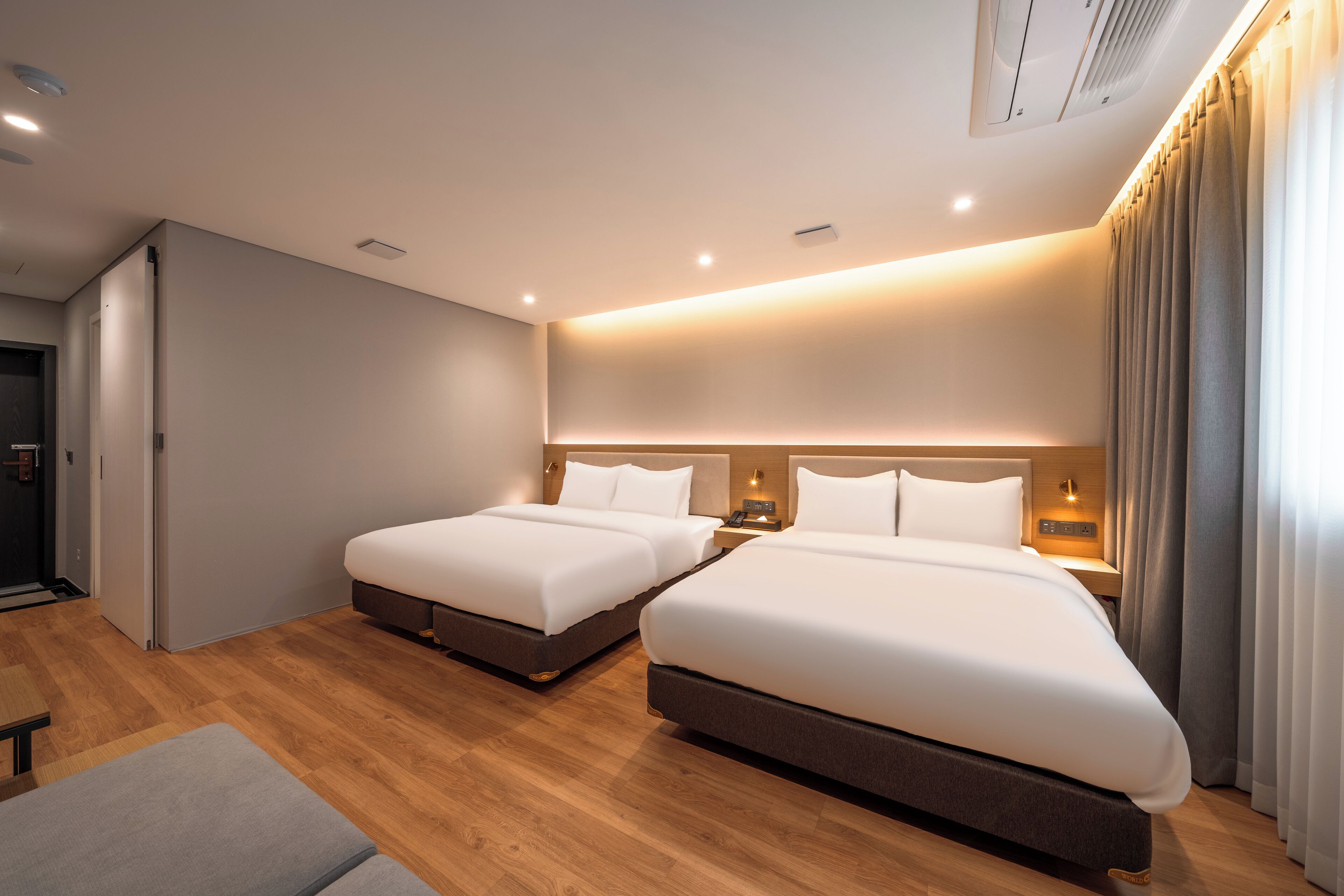 Quarto de hotel moderno com duas camas, piso de madeira e cores neutras.