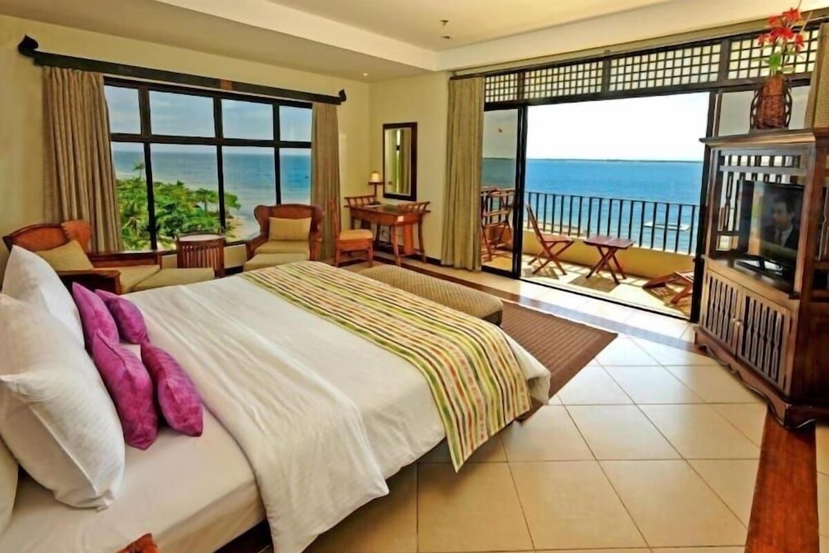 Quarto de hotel com uma cama grande, televisão e varanda com vista para o mar.