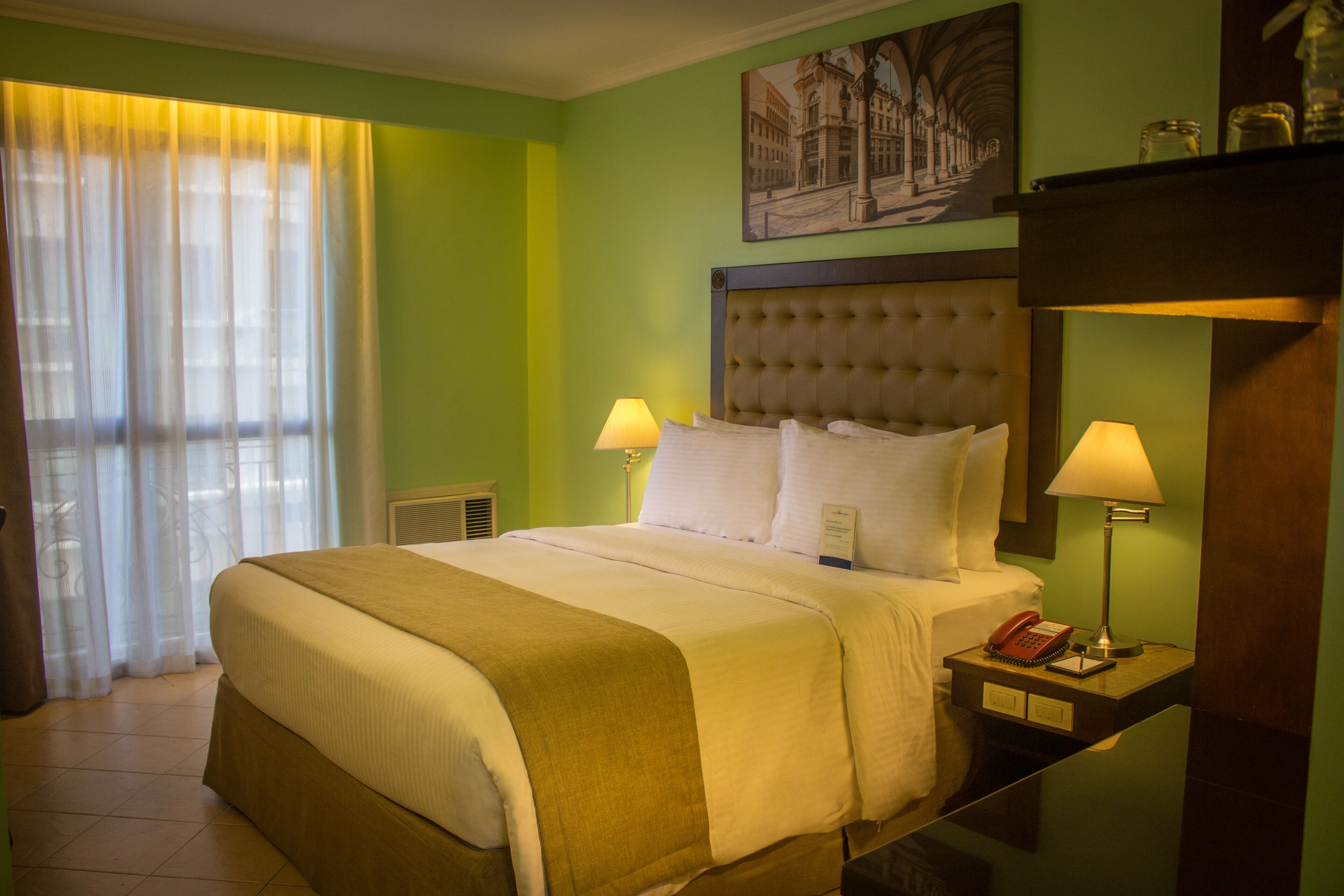 Quarto de hotel com uma cama grande, duas luminárias de cabeceira, um telefone e um quadro na parede.