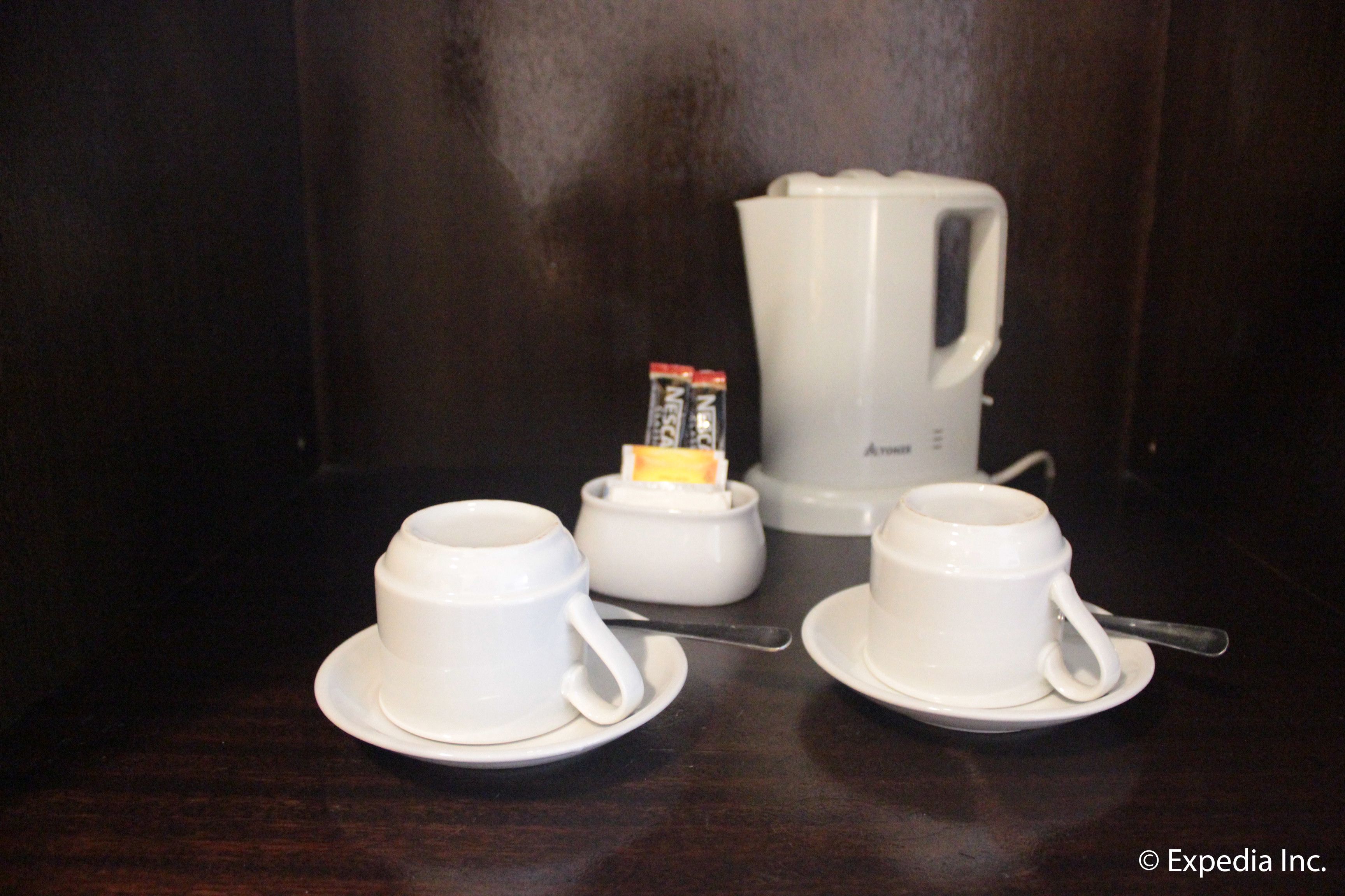 Uma mesa com três xícaras e pires brancos, uma pequena caixa de chá e uma chaleira elétrica branca.