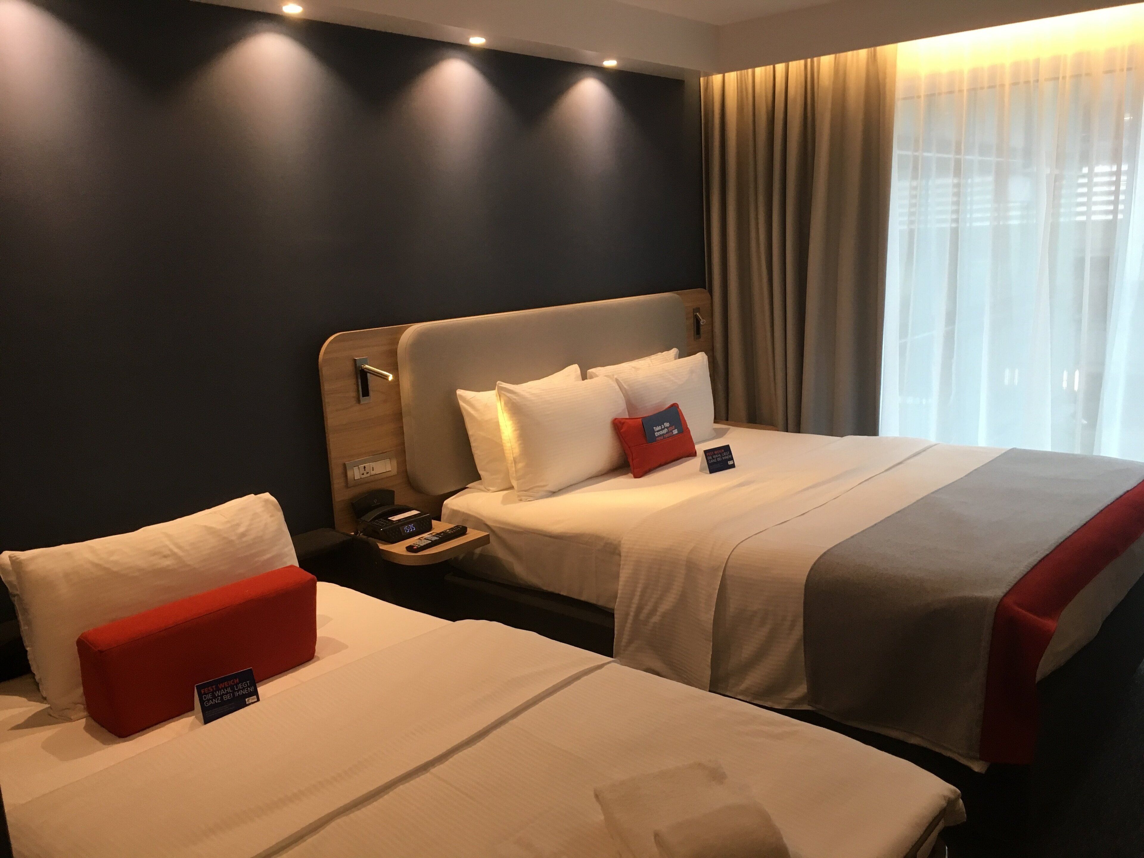 Quarto de hotel com duas camas, uma mesinha de cabeceira com controle remoto e uma janela com cortinas.