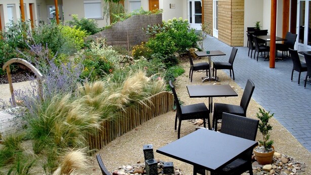 Um pátio com mesas ao ar livre, um jardim de pedras e diversas plantas.