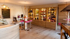 Uma área de bar com prateleiras de madeira repletas de garrafas, um cardápio em lousa e banquetas cor-de-rosa.