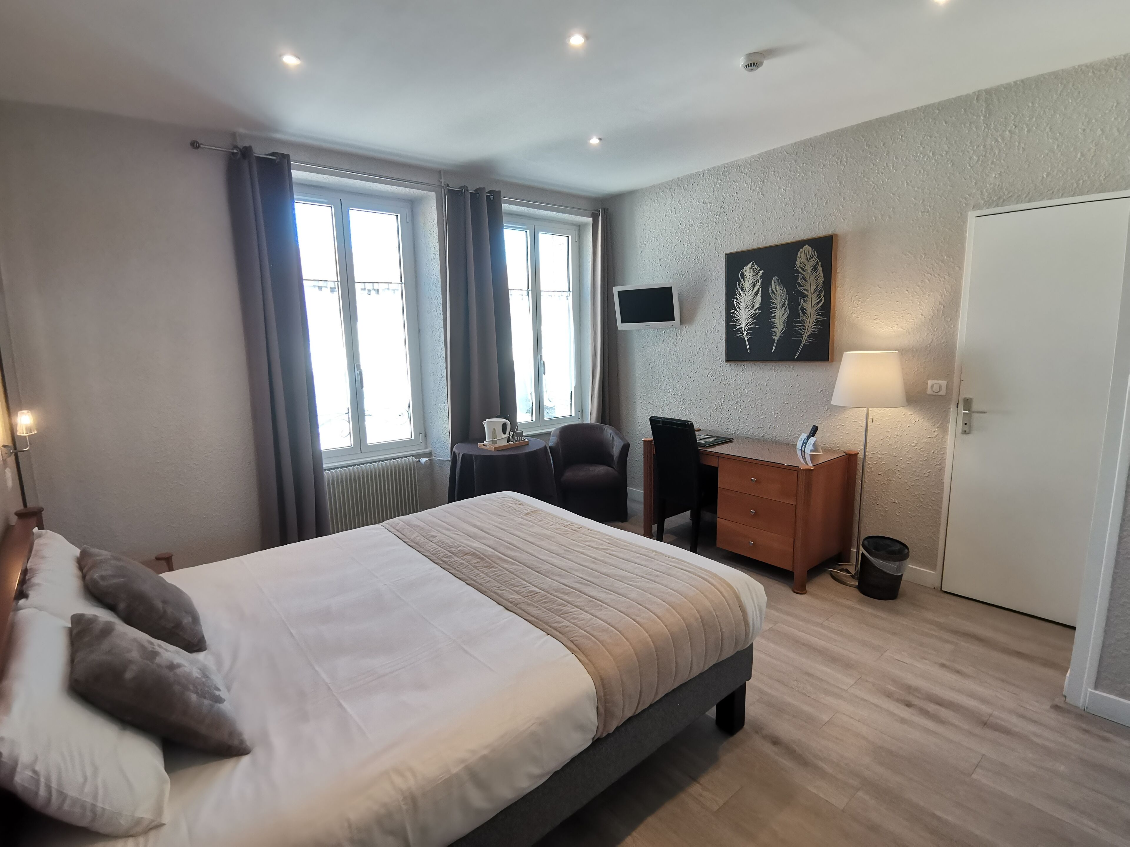 Quarto de hotel com cama, escrivaninha, cadeira, luminária, televisão e um quadro na parede.