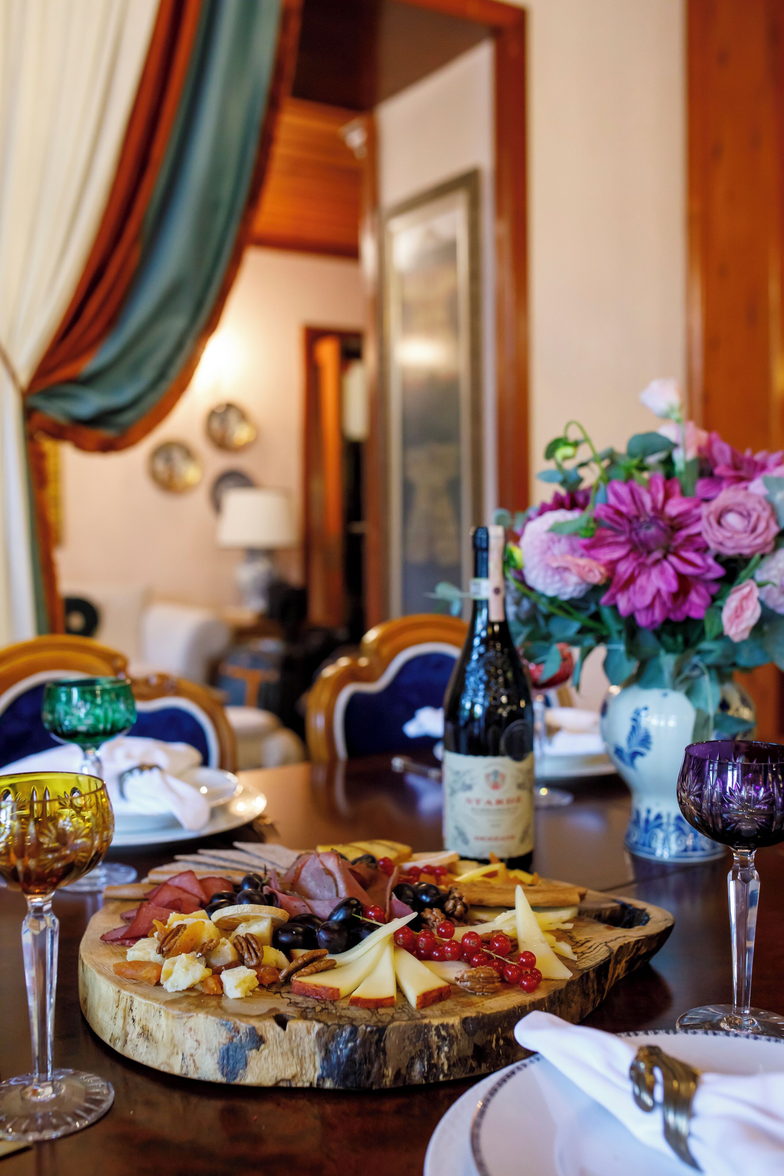 Uma mesa de jantar com uma tábua de queijos, garrafa de vinho e flores.