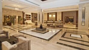 Um hall amplo com área de estar central, balcão de recepção e um lustre moderno.