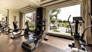 Uma academia com diversos equipamentos de exercício, amplas janelas e vista para o exterior.