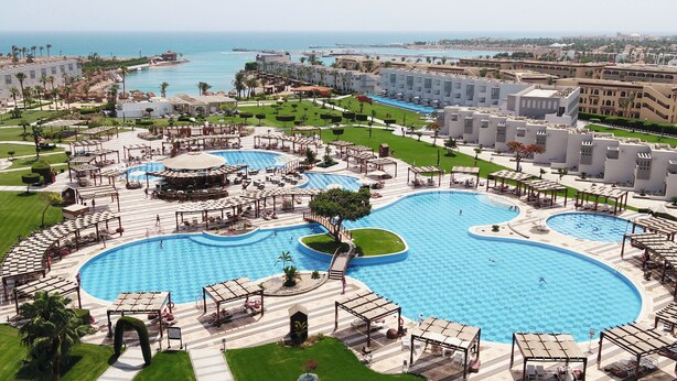 Um resort com várias piscinas, espreguiçadeiras e vista para o mar.