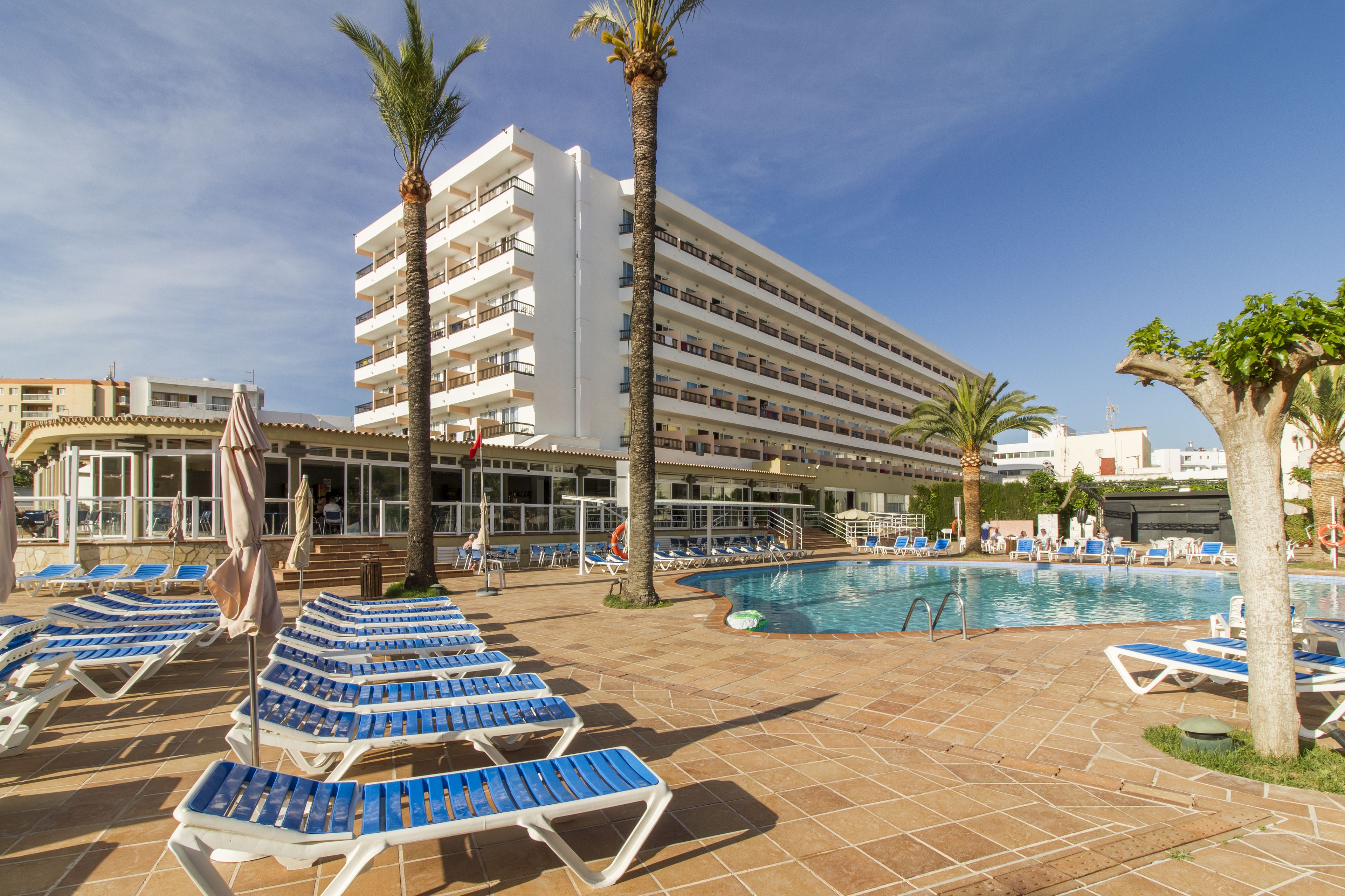 Hotel com piscina, espreguiçadeiras e palmeiras.
