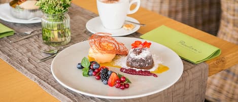Um prato de sobremesas com doces variados e uma xícara de café sobre uma mesa de madeira.