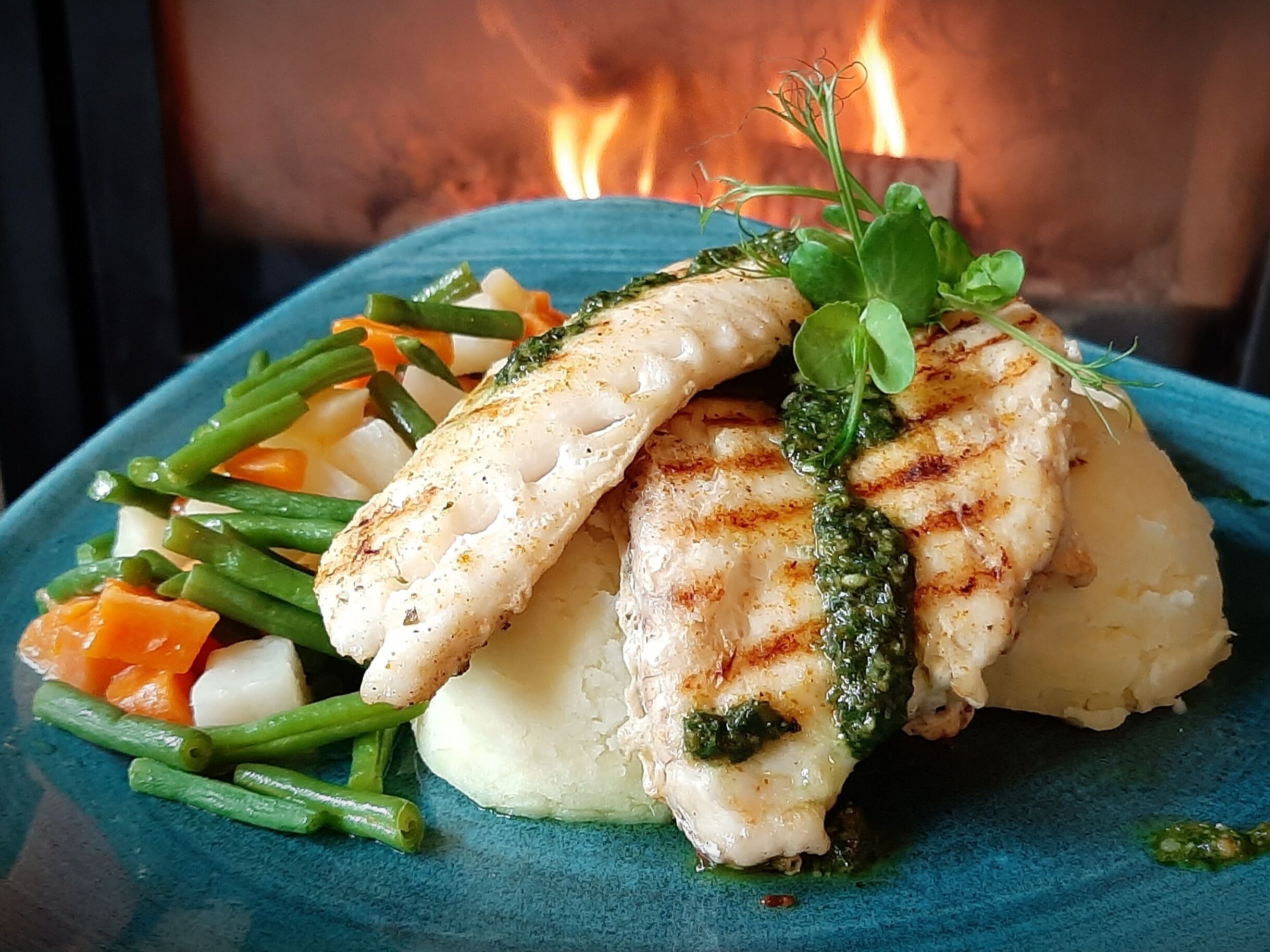 Prato de peixe grelhado com vagem e batatas, guarnecido com ervas, servido em um prato azul.