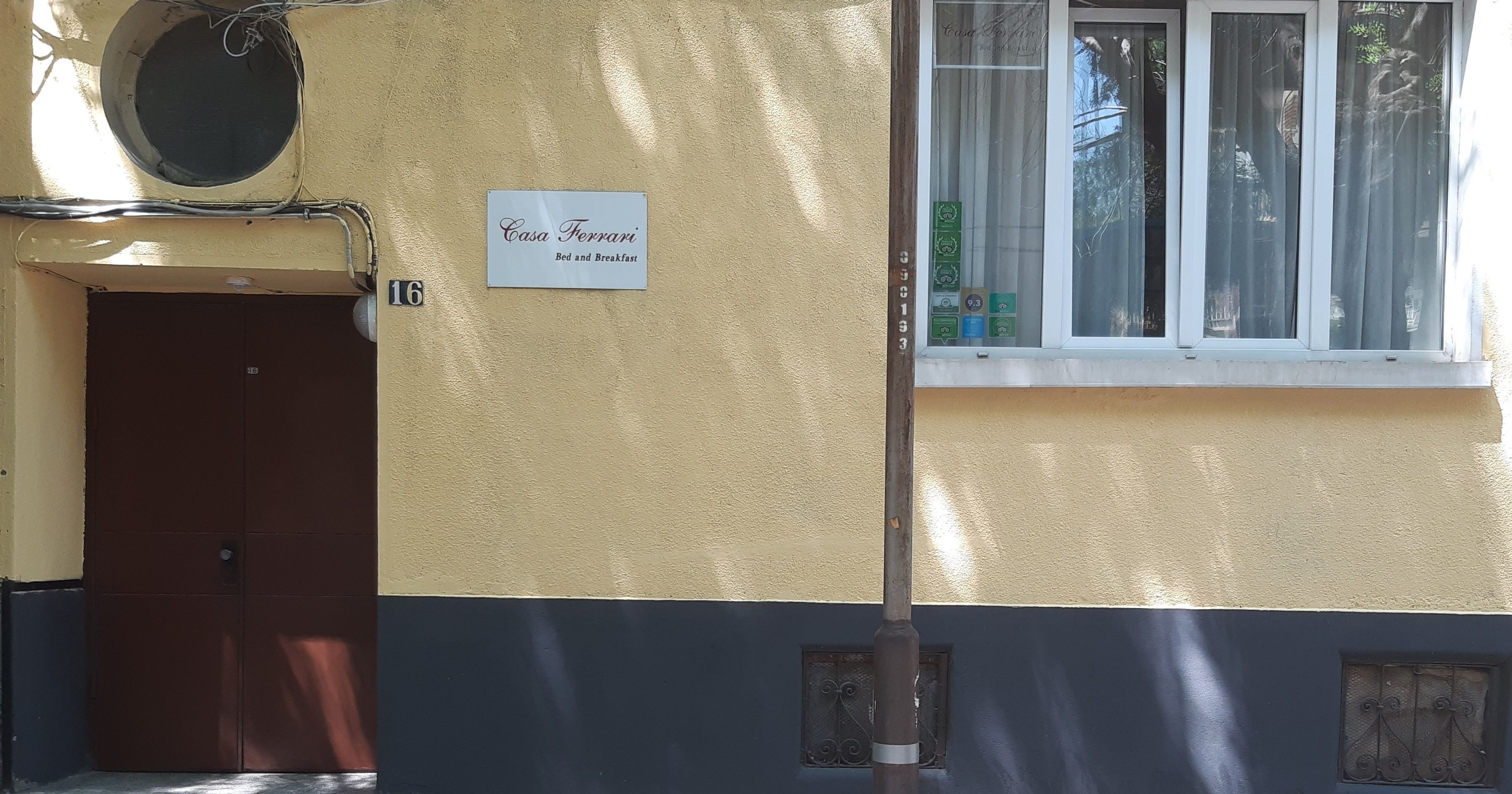 Entrada de um prédio com uma placa que diz 'Casa Ferrari Bed and Breakfast', uma porta marrom e uma janela com cortinas.