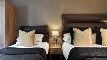 Quarto de hotel com duas camas, cada uma com cabeceira, mesa de cabeceira e luminária, além de um guarda-roupa.