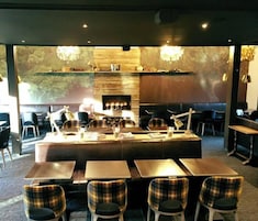 Um restaurante com área de bar central, diversas opções de assento incluindo mesas e cadeiras, e uma lareira ao fundo.