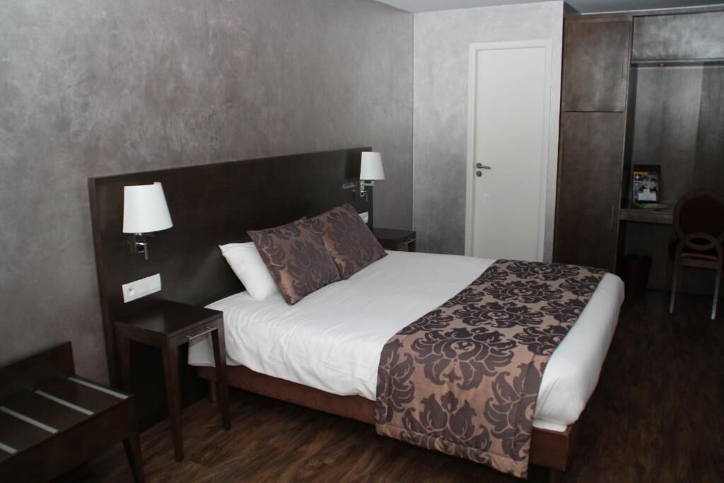Quarto de hotel com cama, abajures, escrivaninha e uma cadeira.