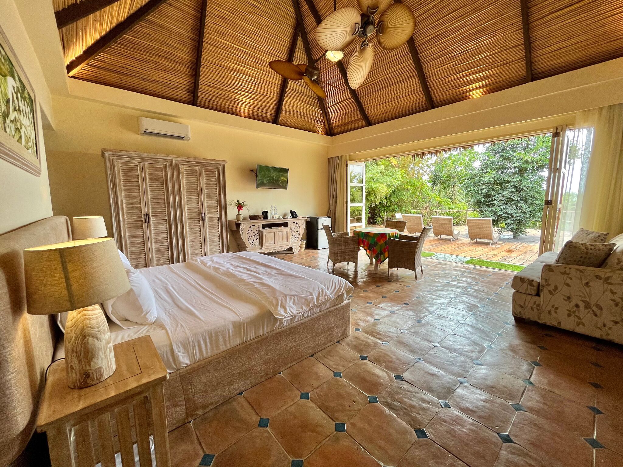 Um quarto espaçoso com uma cama grande, uma escrivaninha e varanda com área de estar ao ar livre.