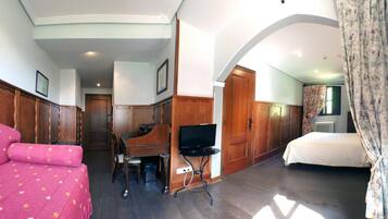 Quarto de hotel com cama, secretária com televisão, piano e área de duche.
