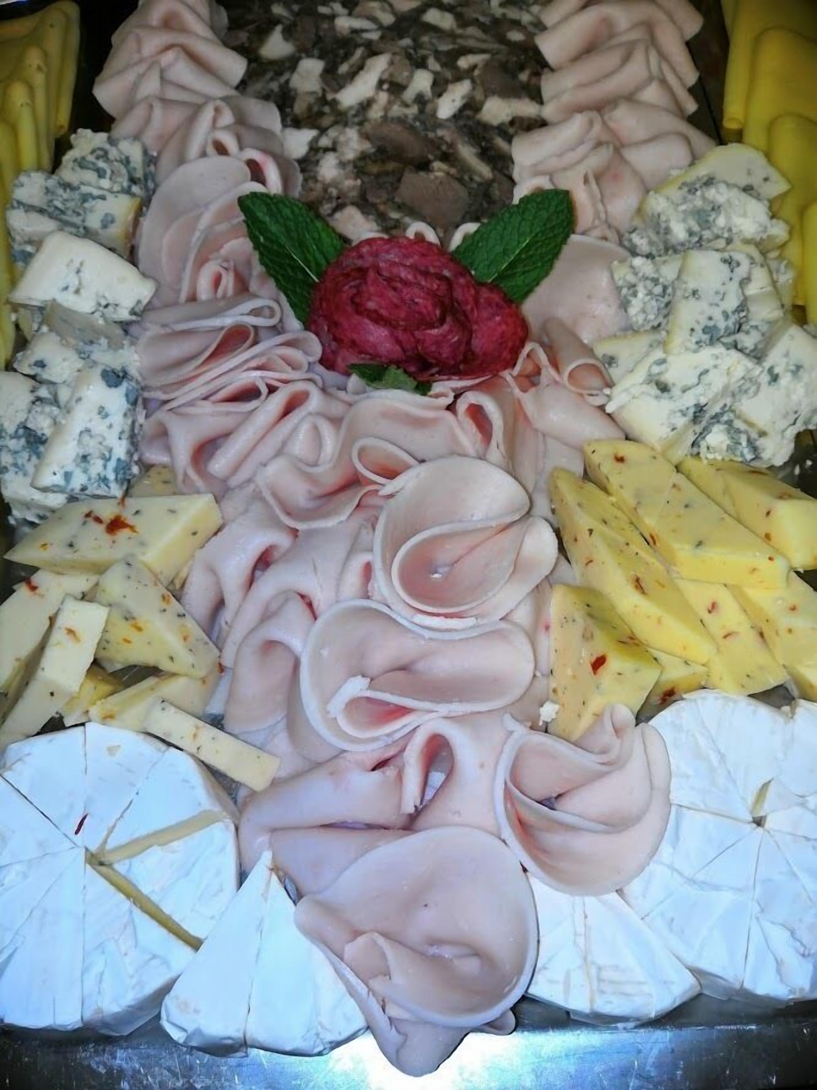 Uma tábua de frios com diversos embutidos, queijos e uma flor decorativa.