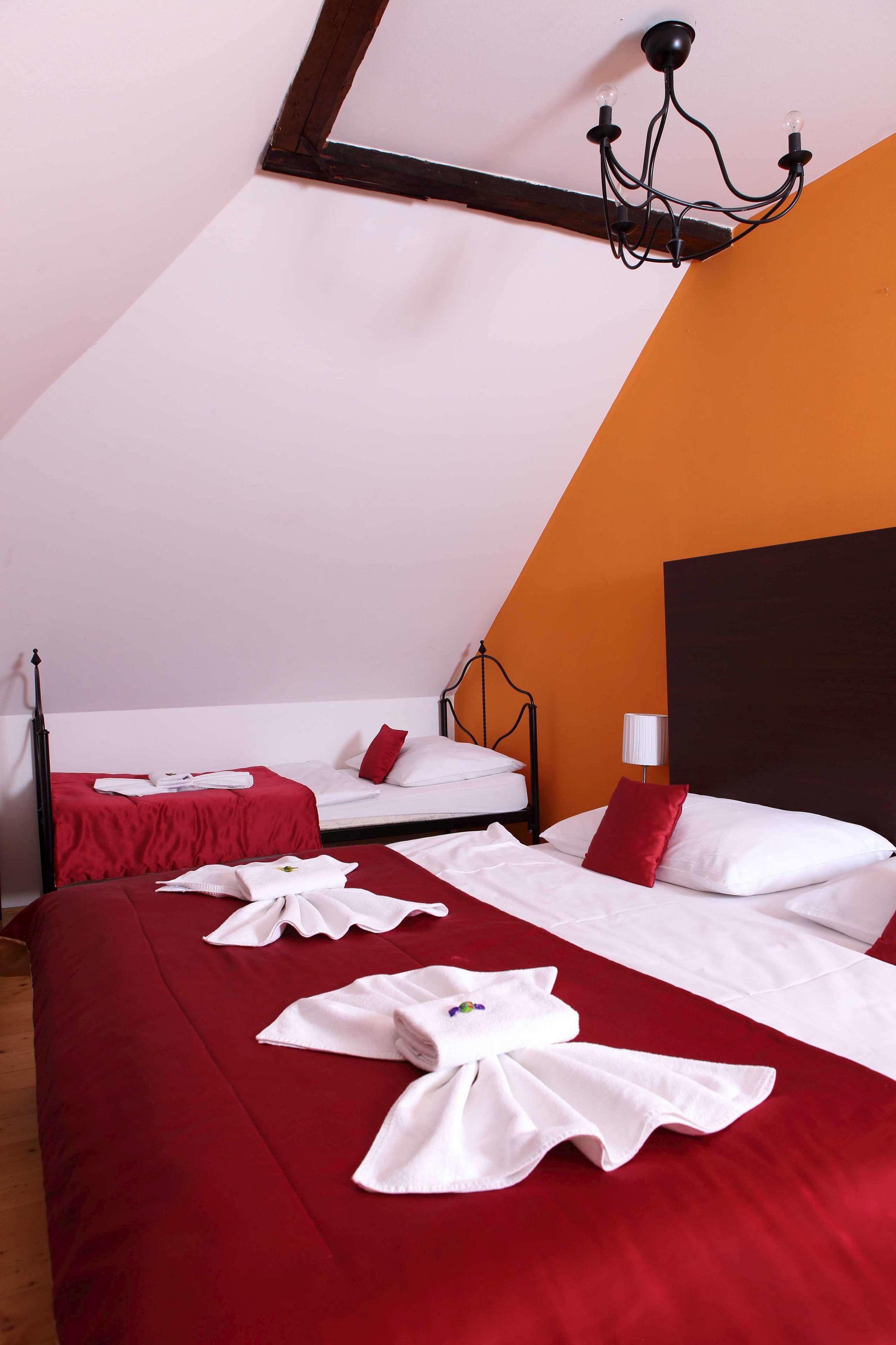 Quarto de hotel com duas camas, roupa de cama vermelha e branca, um candelabro e design moderno.