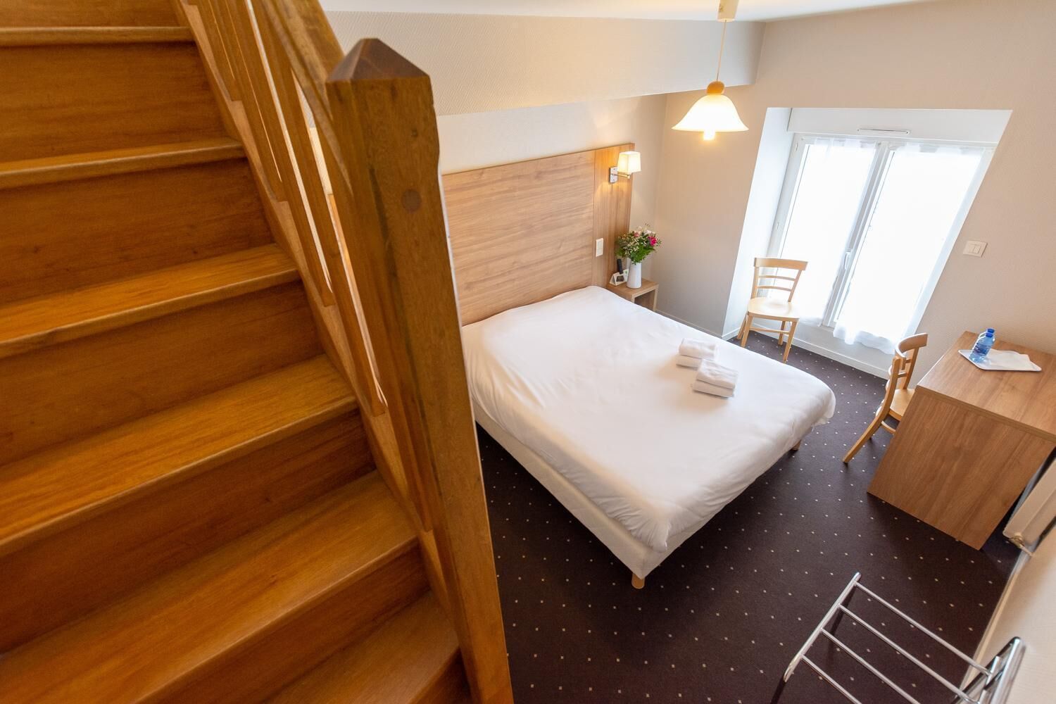 Quarto com escada de madeira, cama com roupa de cama branca, escrivaninha e uma cadeira.