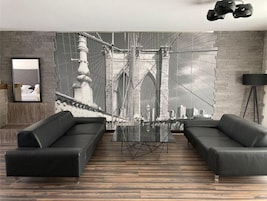 Uma sala de estar moderna com uma grande fotografia em preto e branco de uma ponte, dois sofás pretos, uma mesa de centro de vidro e um abajur de chão preto.