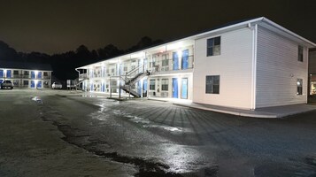 Um motel com uma escadaria central, vários quartos com portas azuis e um estacionamento.