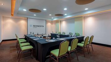 Uma sala de conferências com uma mesa comprida, cadeiras verdes e um quadro branco com o texto 'SONESTA CUSCO'.