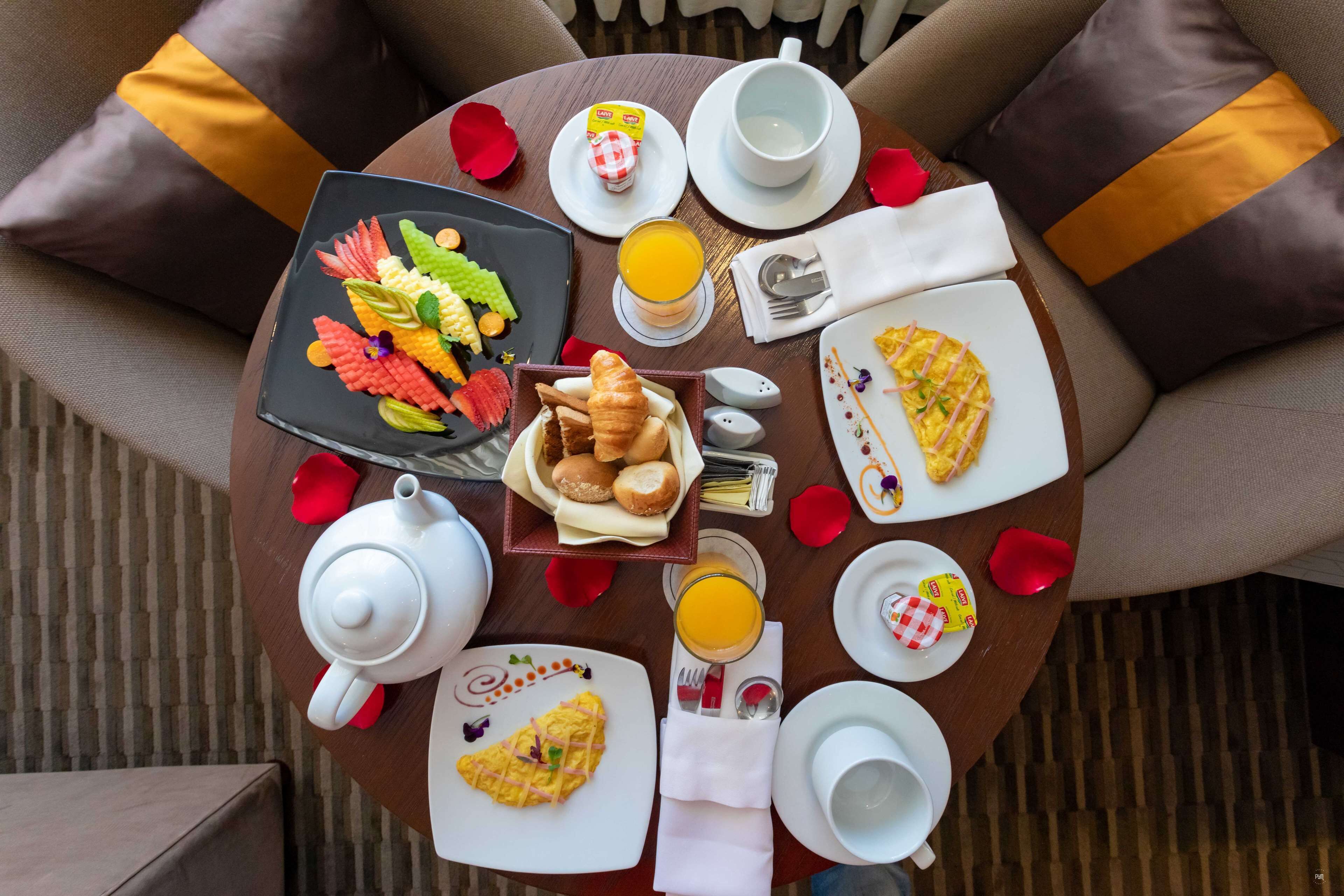 Uma mesa redonda com uma variedade de alimentos para o café da manhã, incluindo doces, um omelete e uma bandeja de frutas.
