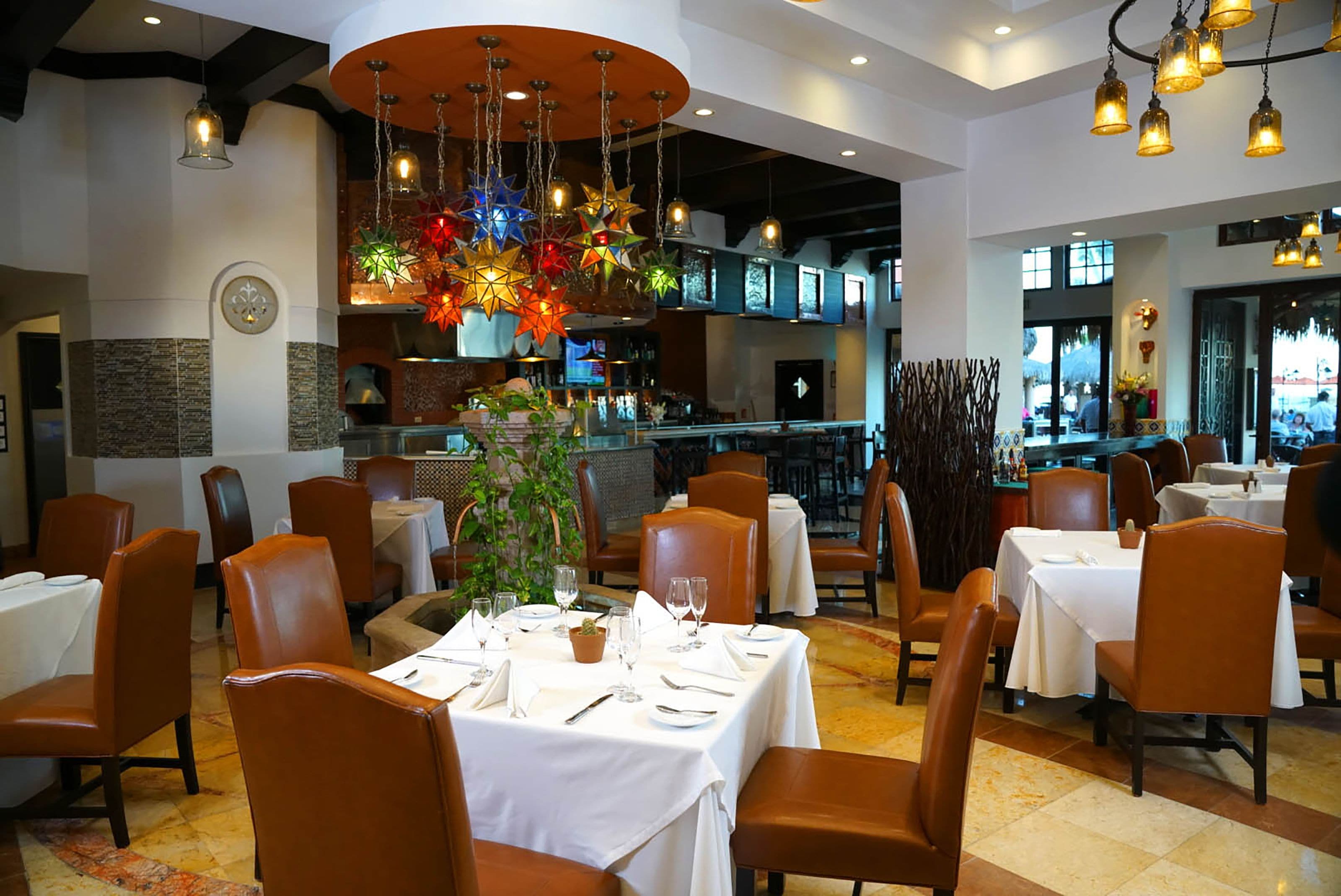 Um restaurante com mesas preparadas para refeições, um bar e um lustre decorativo.