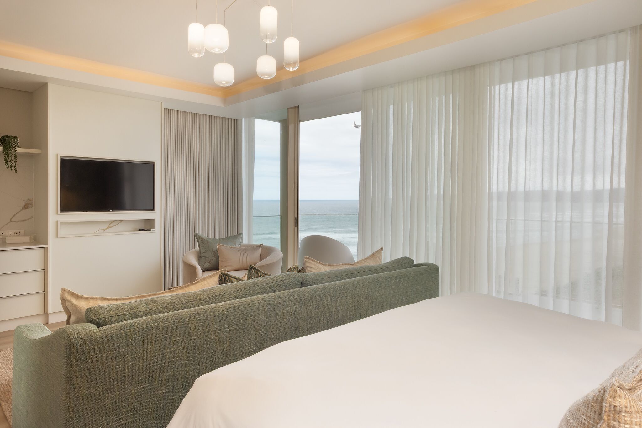 Quarto de hotel com uma cama grande, televisão, área de estar com vista para o oceano e varanda.