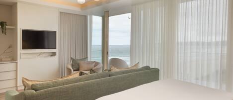 Quarto de hotel com uma cama grande, televisão, área de estar com vista para o oceano e varanda.