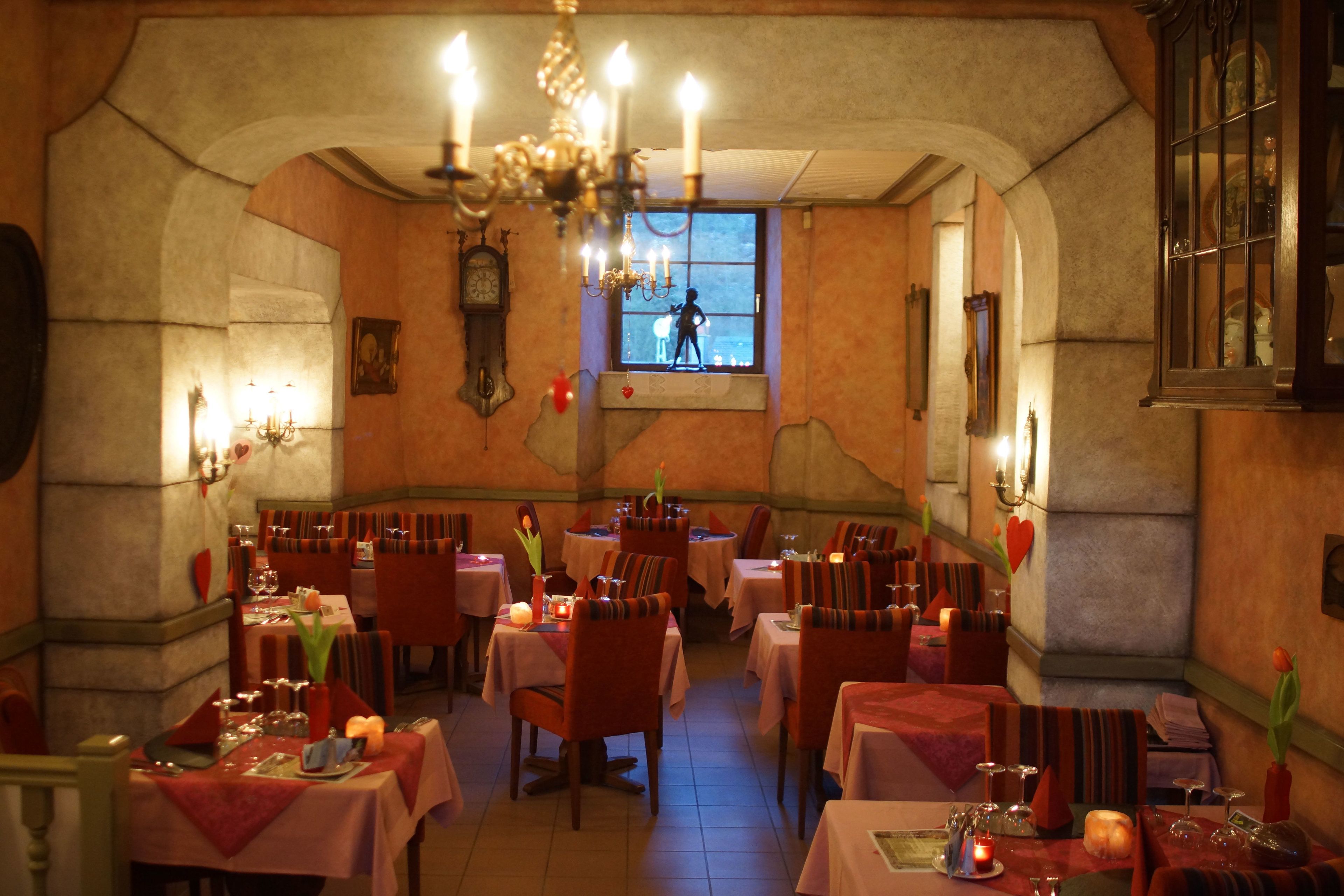 Um restaurante acolhedor com várias mesas e cadeiras, um candelabro e vista para o exterior através de uma janela.
