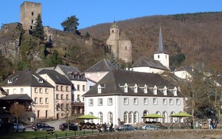 Uma cidade histórica com um castelo imponente numa colina, rodeada por edifícios tradicionais com características arquitetónicas distintas.