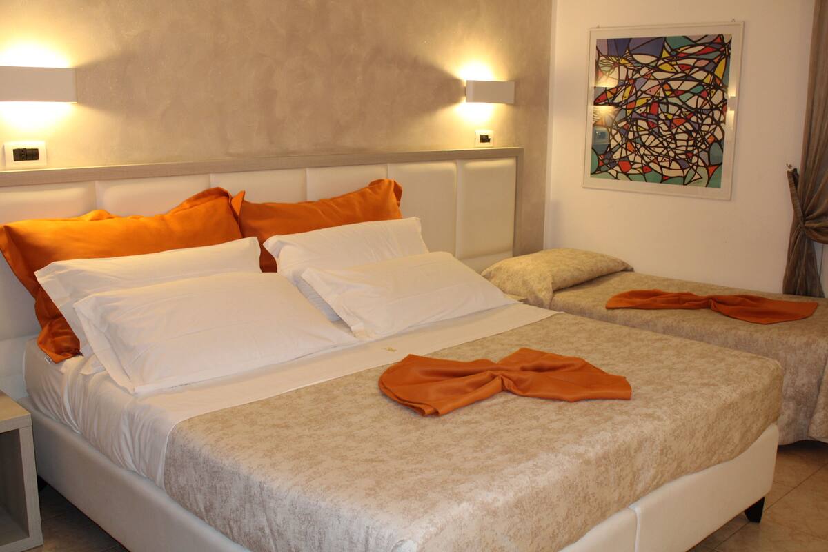 Quarto de hotel com duas camas, cada uma com roupa de cama branca e laranja, cabeceira e uma obra de arte na parede.