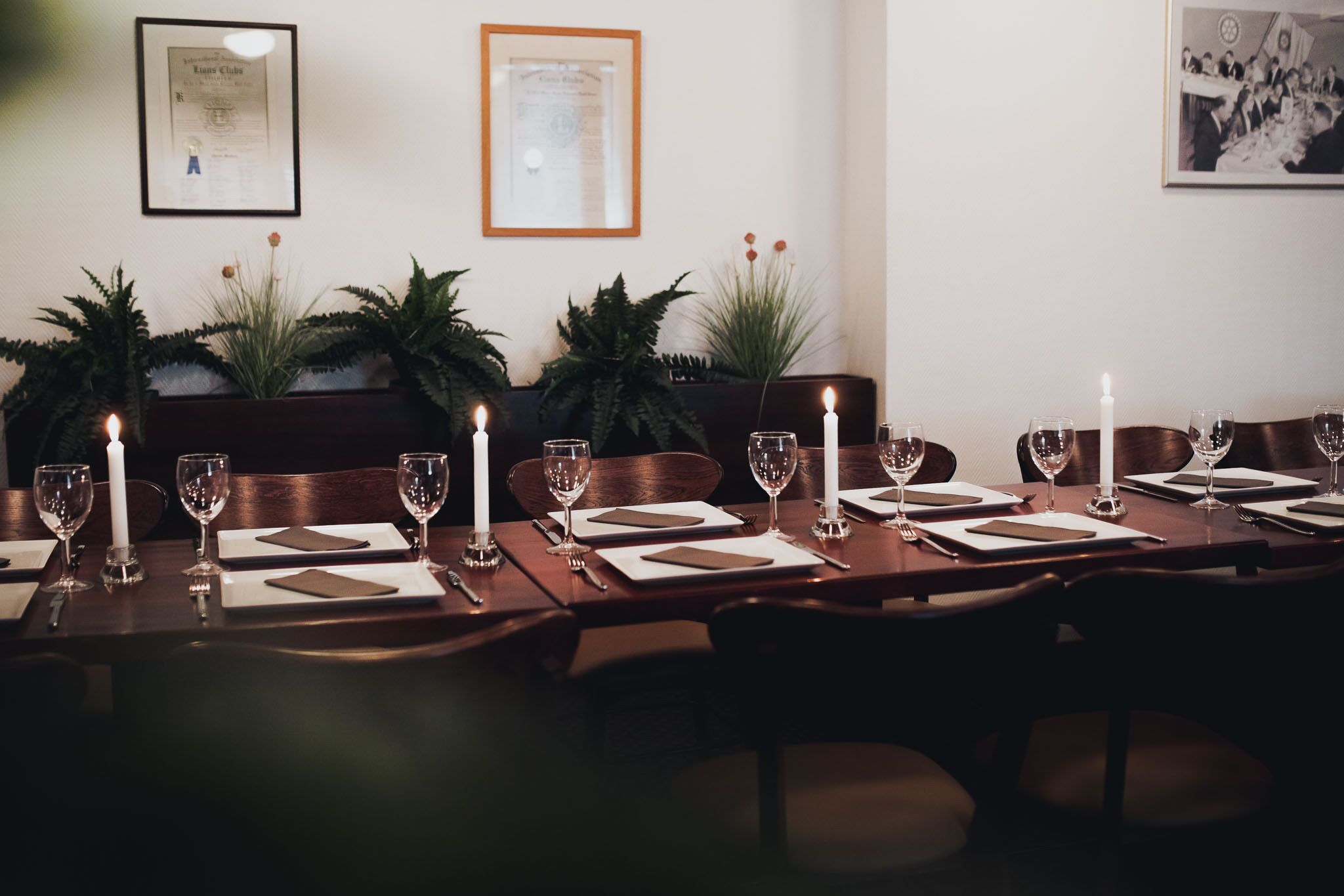 Uma mesa de jantar posta com velas, pratos e talheres, rodeada por cadeiras.