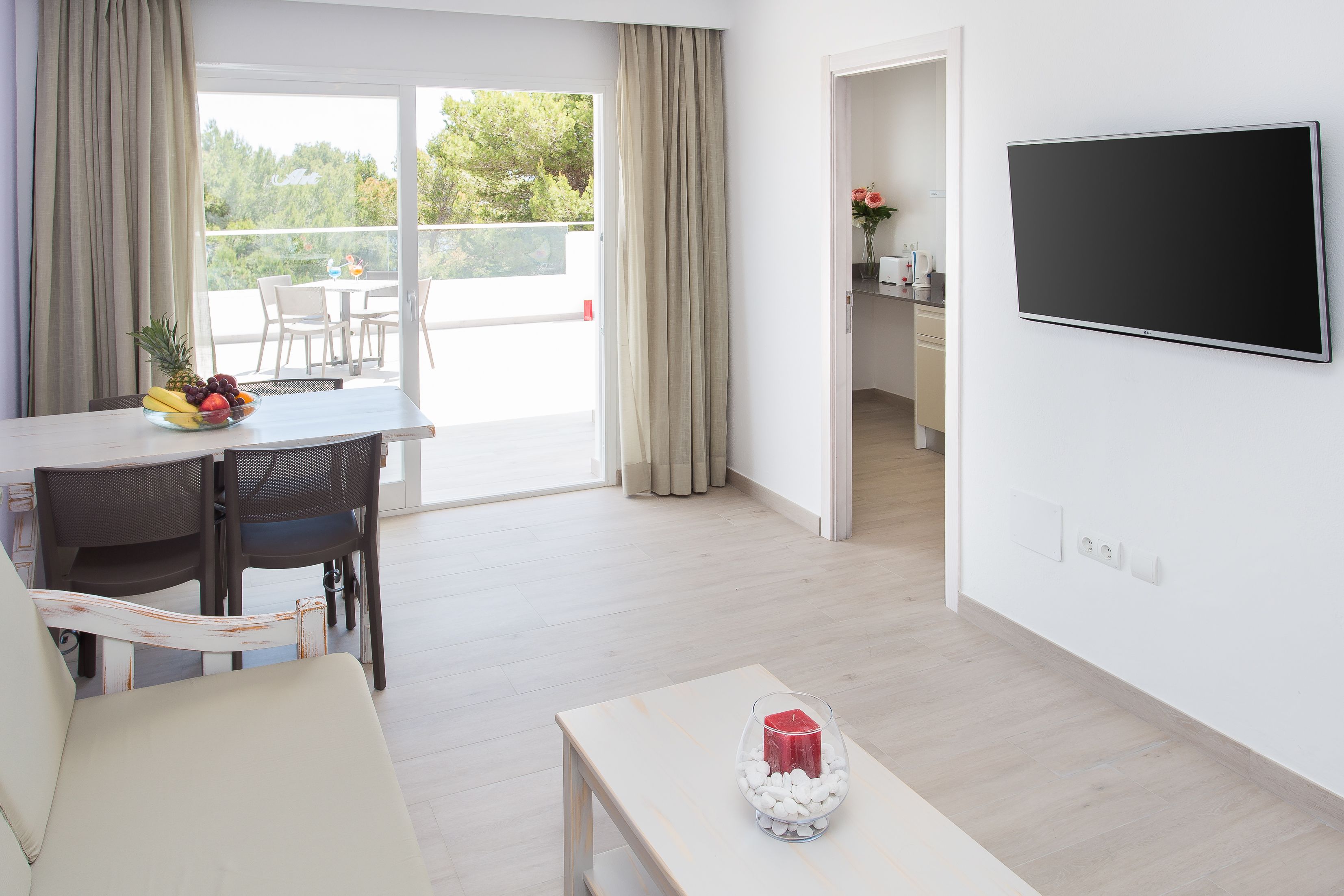 Quarto de hotel moderno com área de jantar, TV e varanda com vista para árvores.