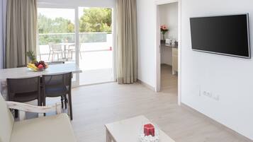 Quarto de hotel moderno com área de jantar, TV e varanda com vista para árvores.