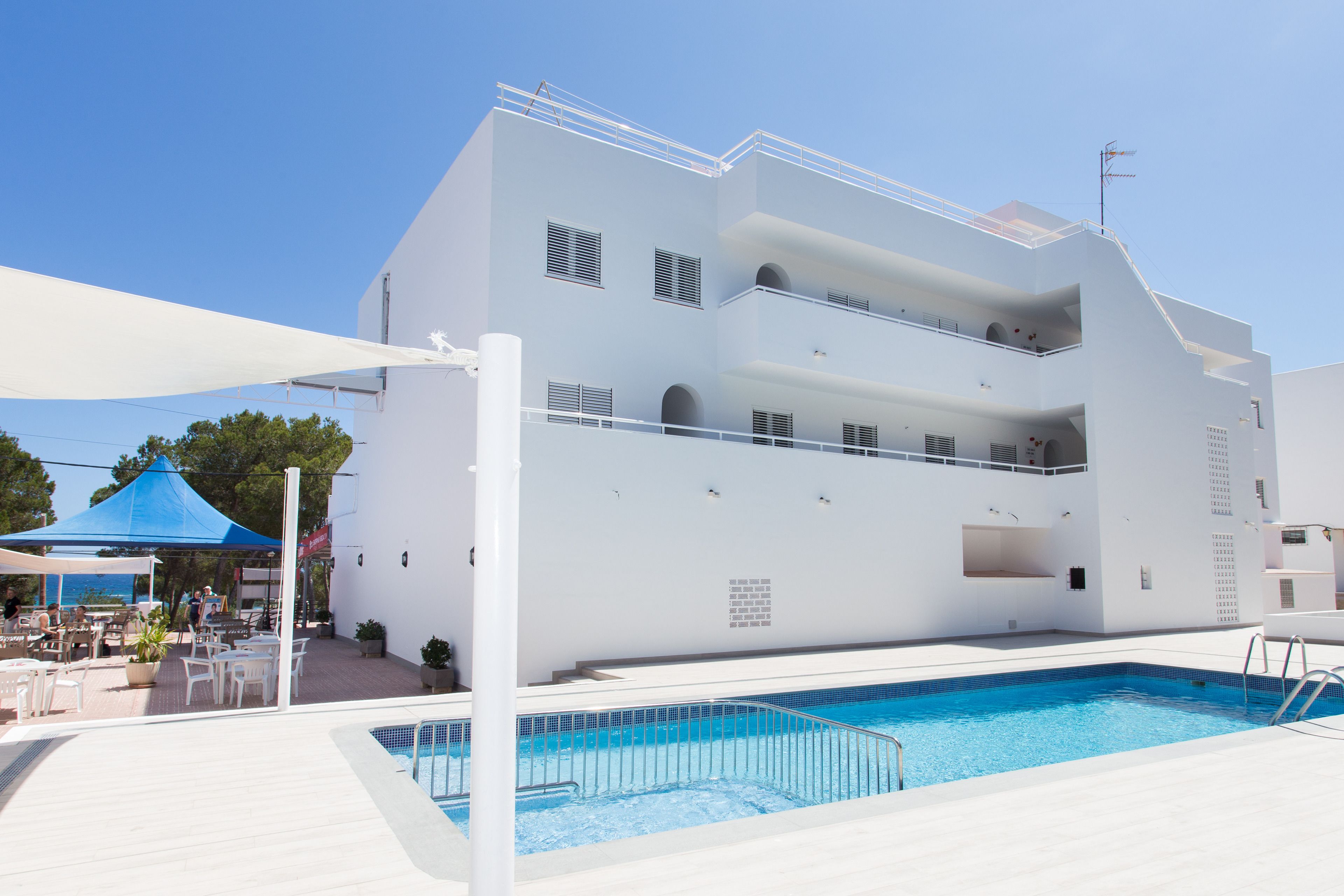 Um edifício moderno com piscina, área de estar ao ar livre e céu azul vibrante.