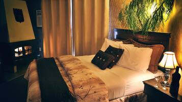 Quarto de hotel com cama, mesa de cabeceira com abajur, planta e cabideiro fixado na parede.