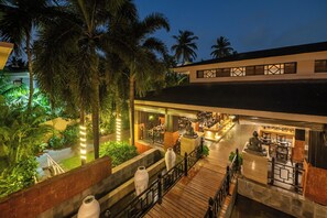 Um hotel com área externa coberta, palmeiras e um espaço para refeições.