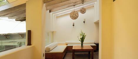 Um interior moderno com um banco de madeira, uma mesa pequena com um vaso e uma área de estar com almofadas.