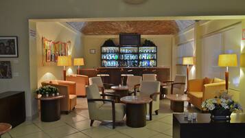 Um saguão de hotel com áreas de estar, um bar e uma tela de televisão.
