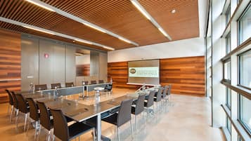 Sala de conferências com uma mesa comprida, cadeiras, tela de projetor e teto de madeira.