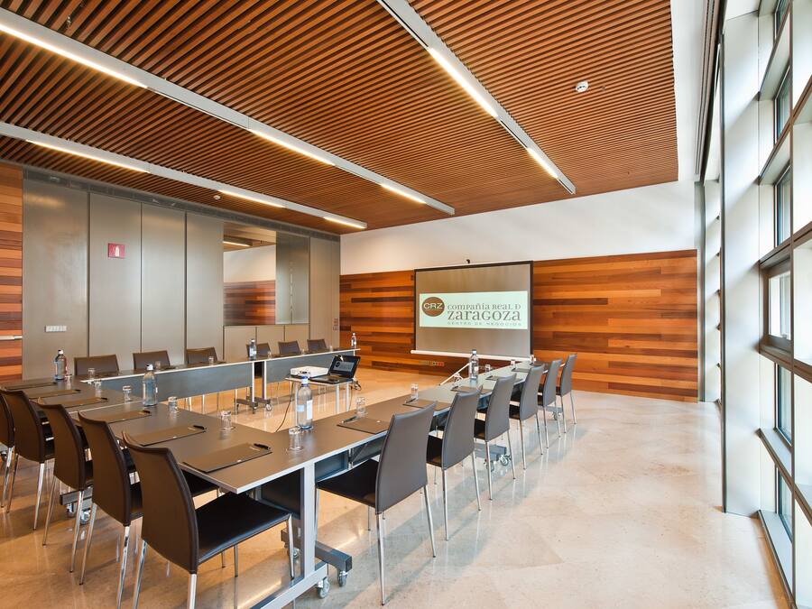 Sala de conferências com uma mesa comprida, cadeiras, tela de projetor e teto de madeira.