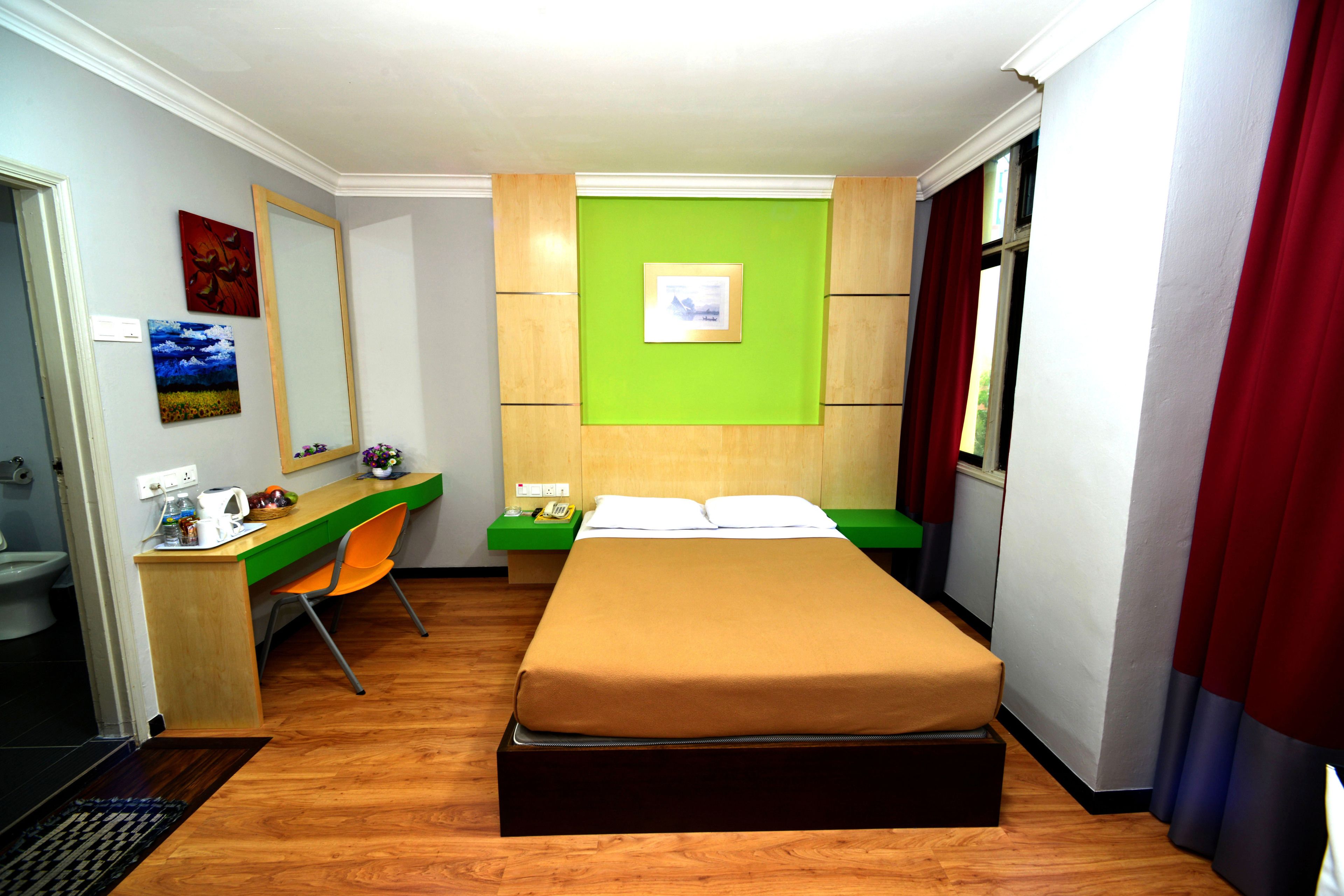 Quarto de hotel com cama, escrivaninha com cadeira, pia e janela com cortinas.